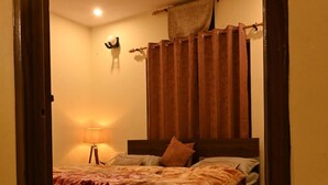 Quarto com cama de madeira, cabeceira, mesa de cabeceira e cortina.