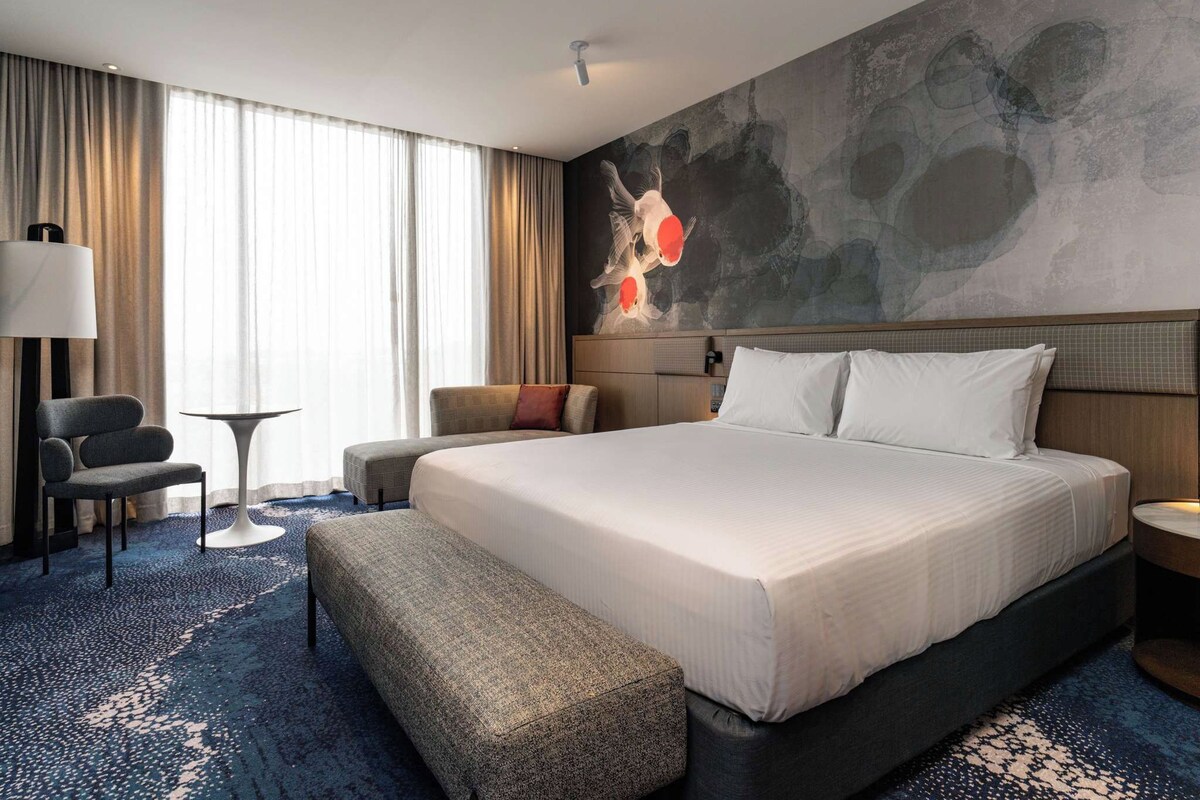 Quarto de hotel com uma cama grande, uma escrivaninha, uma cadeira e uma pequena mesa.