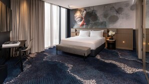 Quarto de hotel moderno com uma cama grande, uma mesa de trabalho e vista para a cidade.
