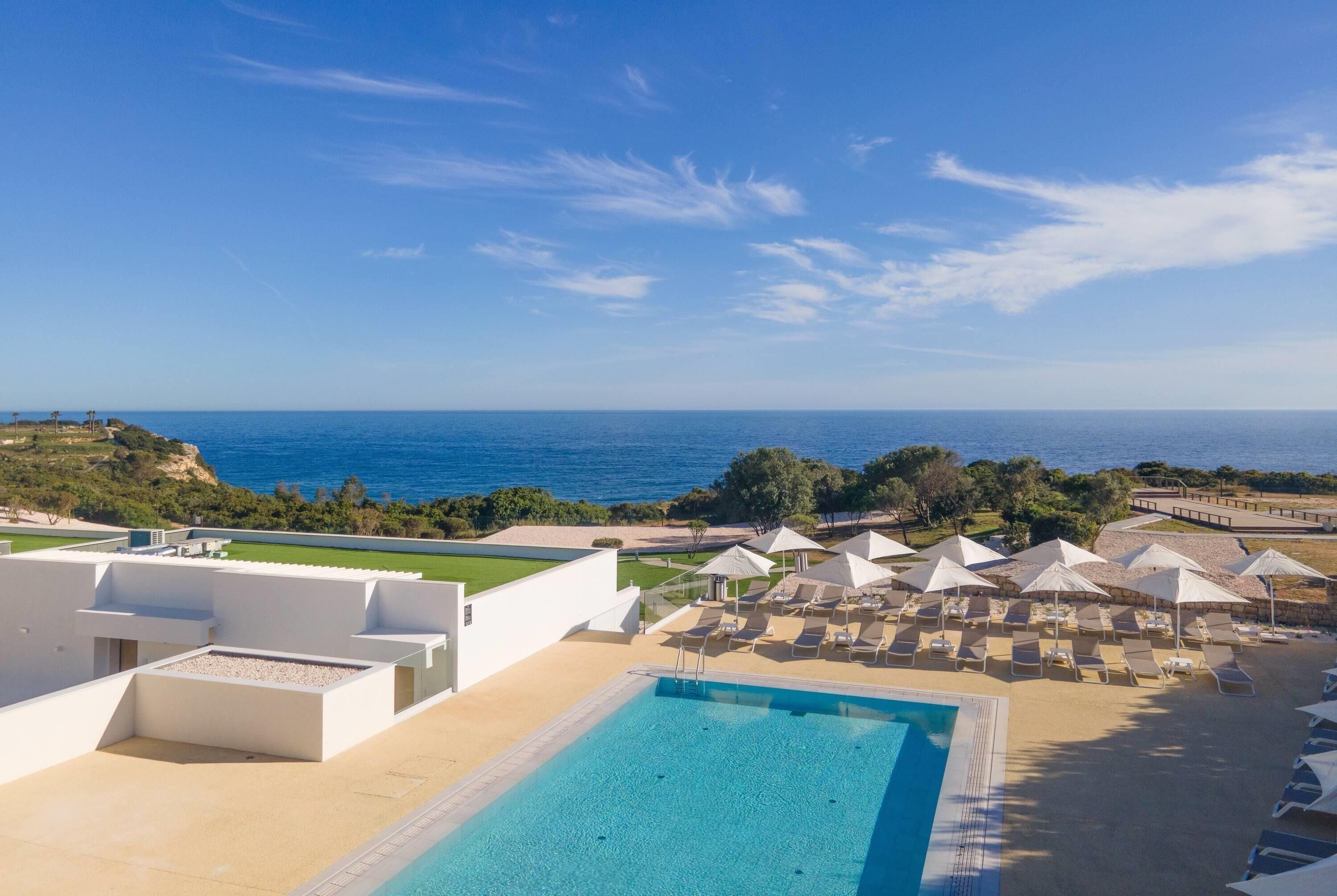 Piscina com vista para o mar, cadeiras de espreguiçadeira e guarda-sóis.