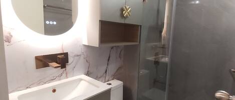 Uma casa de banho moderna com uma sanita branca, uma loiça e um compartimento de duche com divisória de vidro.