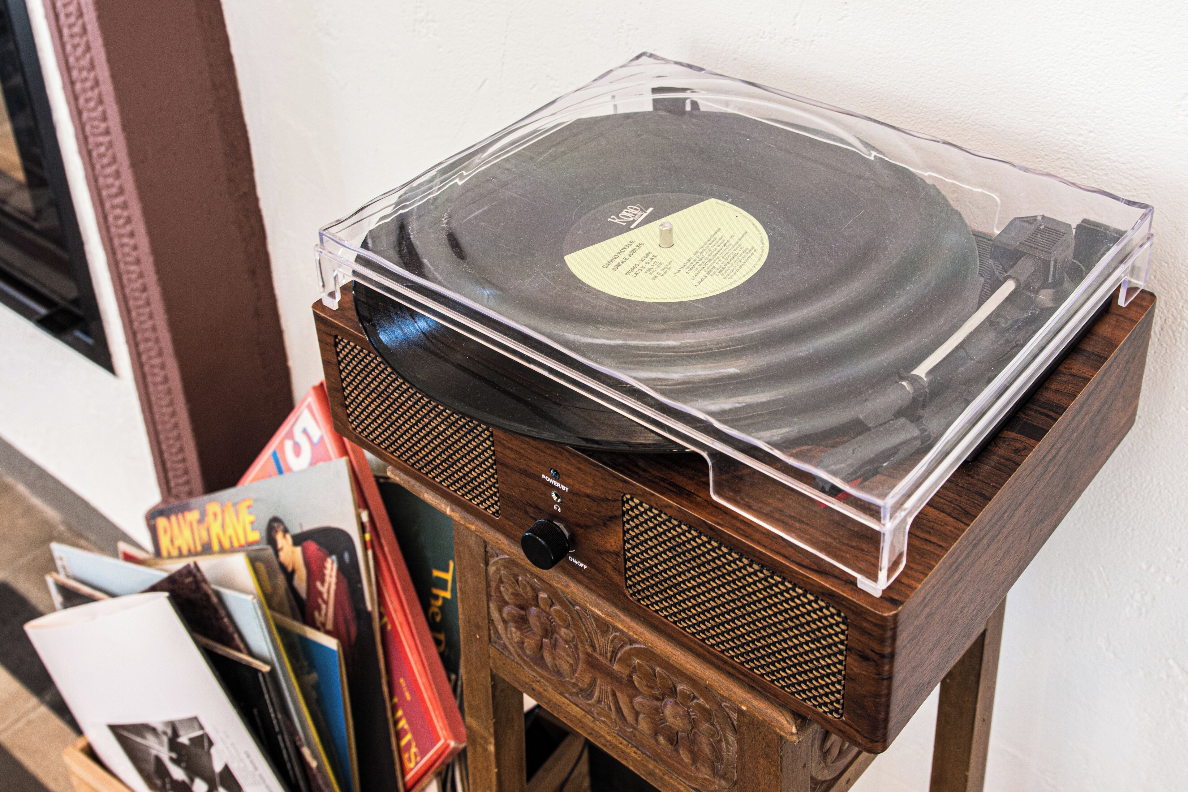 Um toca-discos de madeira com uma tampa de plástico transparente, posicionado sobre uma pequena mesa.