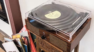 Um toca-discos de madeira com uma tampa de plástico transparente, posicionado sobre uma pequena mesa.