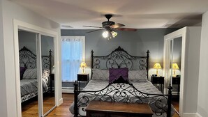 Quarto com cama de dossel, ventoinha no teto, duas mesas de cabeceira com abajures e um banco de madeira.