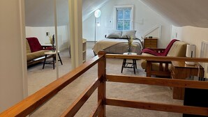 Um quarto de sótão espaçoso com teto inclinado, uma janela grande e uma escada de madeira.