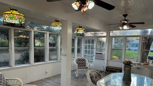 Uma sala de sol com móveis de vime, grandes janelas e luminárias de vidro colorido decorativas.
