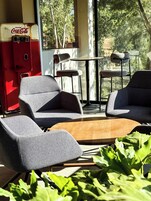 Uma área de estar moderna ao ar livre, com cadeiras cinzas estofadas e uma mesa de centro de madeira.