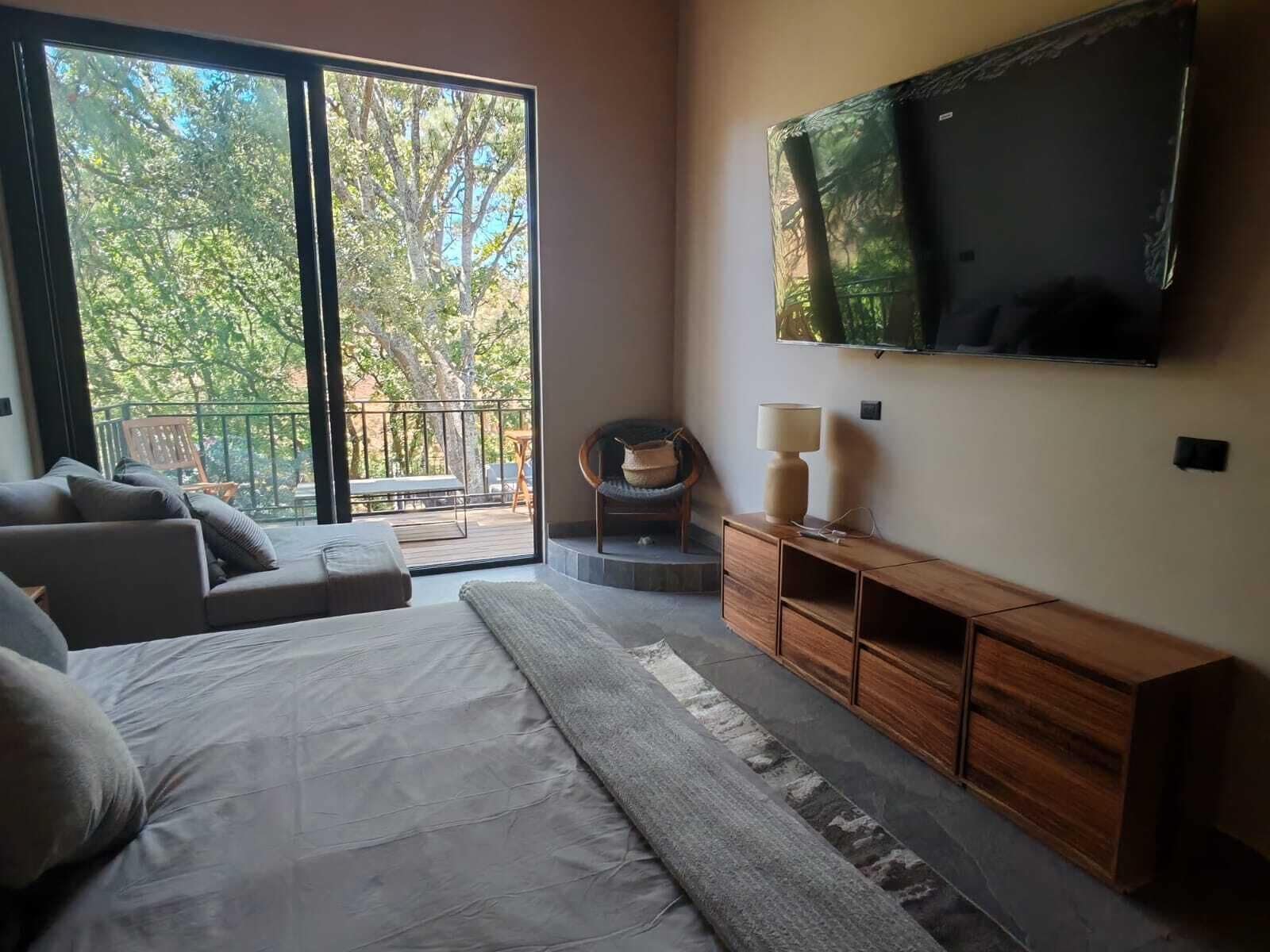 Quarto com uma cama grande, televisão fixada na parede, armário de madeira e vista para o exterior através de uma porta deslizante.