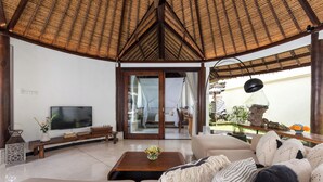 Ampla sala de estar com uma televisão grande, assentos confortáveis e vista para um jardim exterior através de portas de vidro.