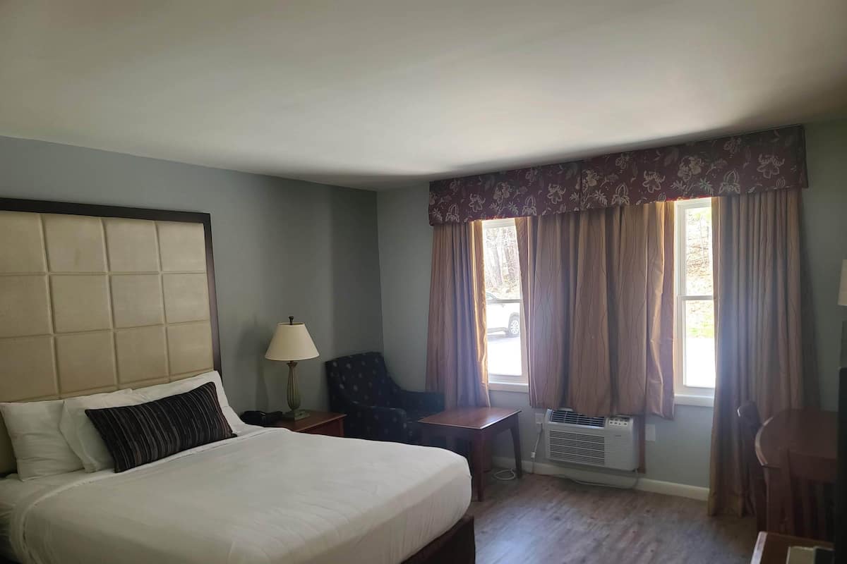 Quarto de hotel com uma cama grande, uma escrivaninha, uma cadeira e uma janela com cortinas.