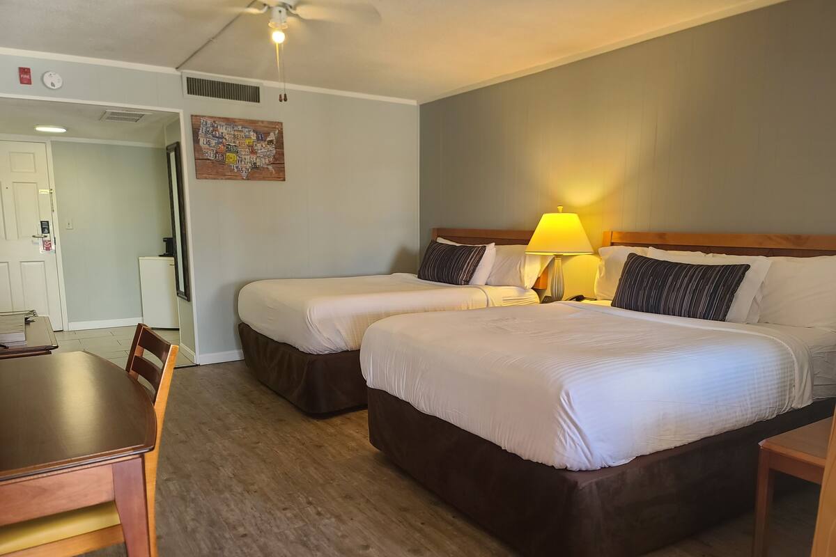 Quarto de hotel com duas camas, uma escrivaninha e uma cadeira.