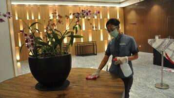 Uma área de recepção de hotel com uma grande orquídea em vaso, um balcão de recepção de mármore e uma parede de madeira com painéis de luz verticais.