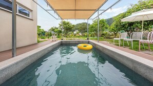 Piscina com boia amarela, cercada por um espaço coberto com área de estar, cadeiras e mesa.