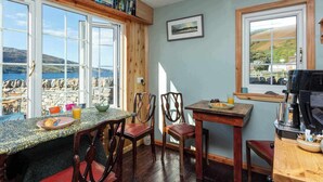 Uma cozinha acolhedora com móveis de madeira, vista para o mar e sala de jantar com mesa posta para dois.