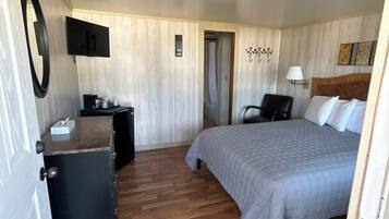Quarto com cama, escrivaninha, cadeira, televisão e porta.