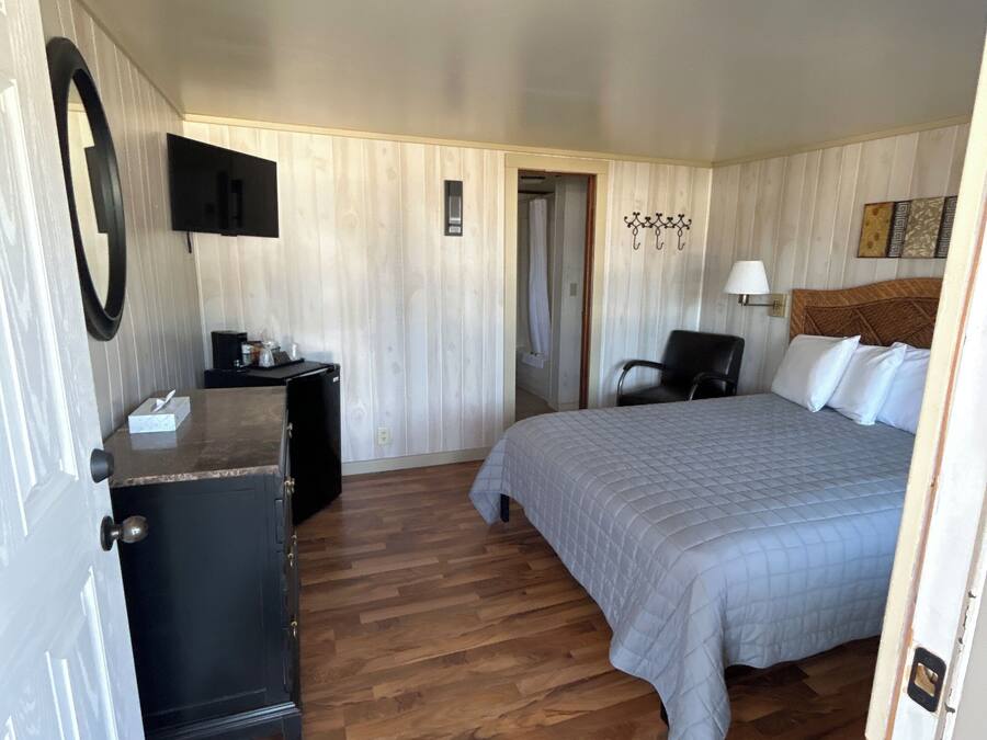 Quarto com cama, escrivaninha, cadeira, televisão e porta.
