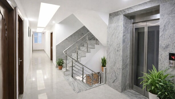 Um hall de hotel moderno com uma escadaria de mármore, um elevador e plantas em vasos.