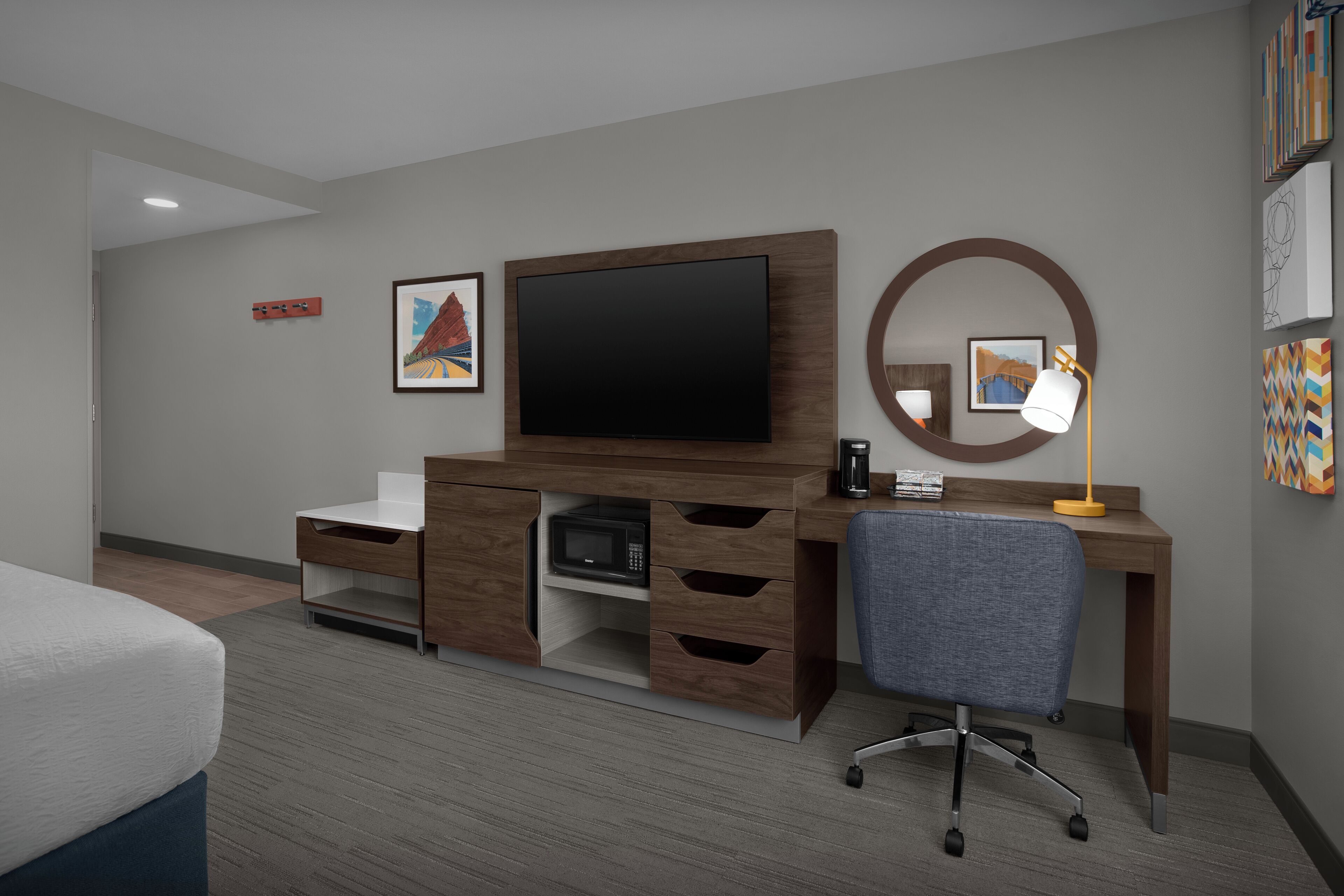 Quarto de hotel com escrivaninha de madeira, televisão de tela plana, micro-ondas, uma cadeira e uma cama.