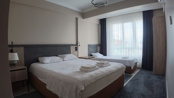 Quarto de hotel com duas camas, mesa de cabeceira, abajur e vista para o exterior pela janela.