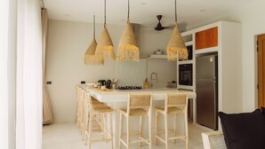 Uma cozinha moderna com uma ilha central, banquetas, luminárias trançadas penduradas e uma geladeira embutida.