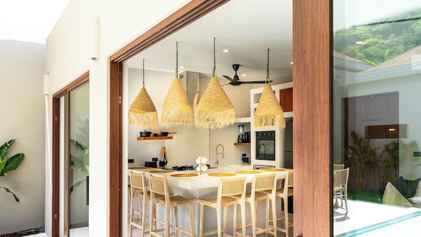 Cozinha moderna com ilha central, luminárias pendentes de vime e vista para o exterior.