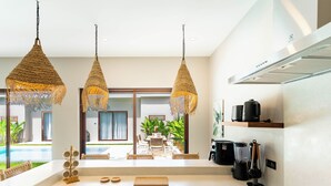 Uma cozinha moderna com luminárias trançadas penduradas, fogão embutido e vista para uma área de jantar com piscina.