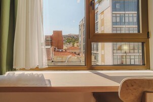 Quarto de hotel com uma grande janela com vista para a paisagem urbana, uma cama e cabeceira de madeira.