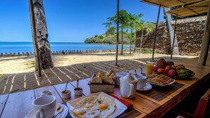 Mesa de café da manhã à beira-mar, com ovos, torradas, frutas e café.