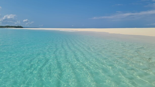 Vista ampla de uma praia com águas azul-turquesa e um litoral distante.