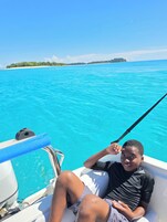 Uma pessoa em um barco com vista para águas turquesa e uma terra ao longe.