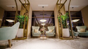Um lobby moderno com área de estar central, grandes espelhos e plantas em vasos.