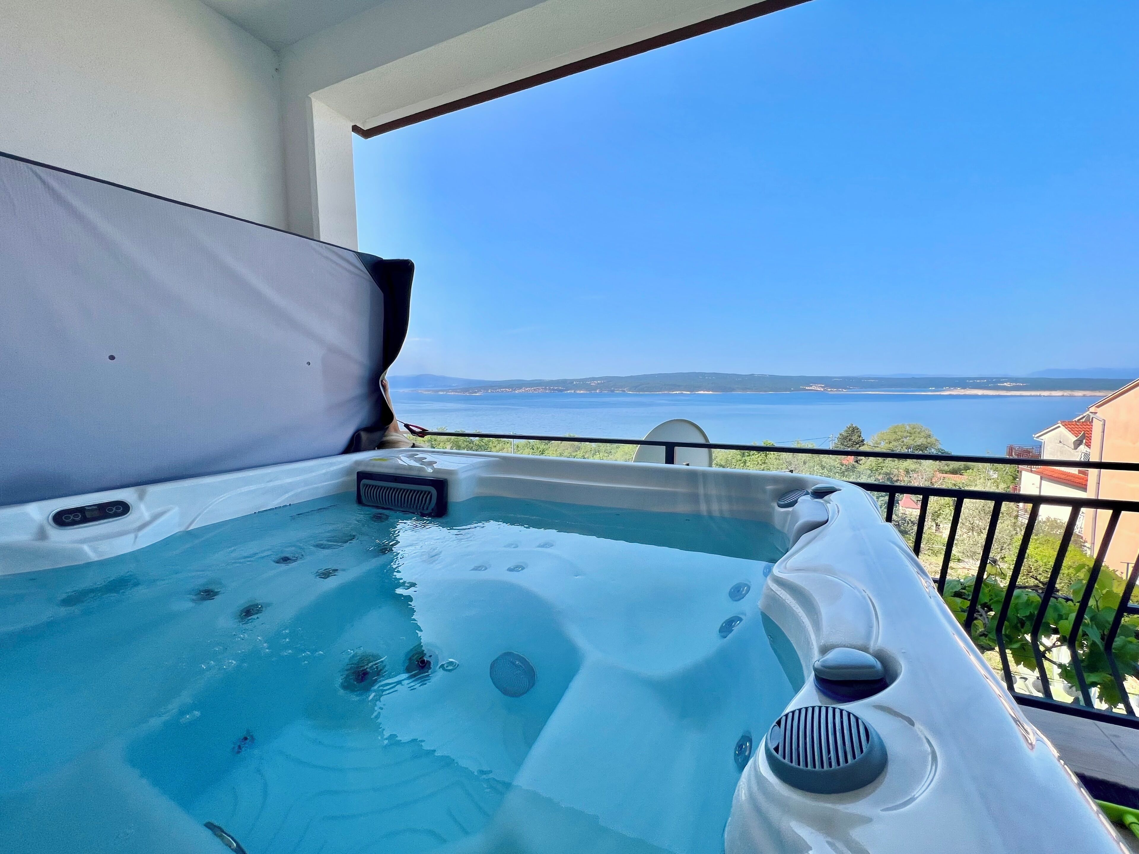 Uma banheira de hidromassagem numa varanda com vista para o mar e colinas ao longe.