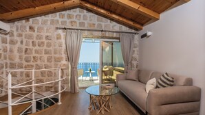 Uma sala de estar aconchegante com parede de pedra, teto de madeira, sofá bege, mesa de centro de vidro e vista para o exterior.