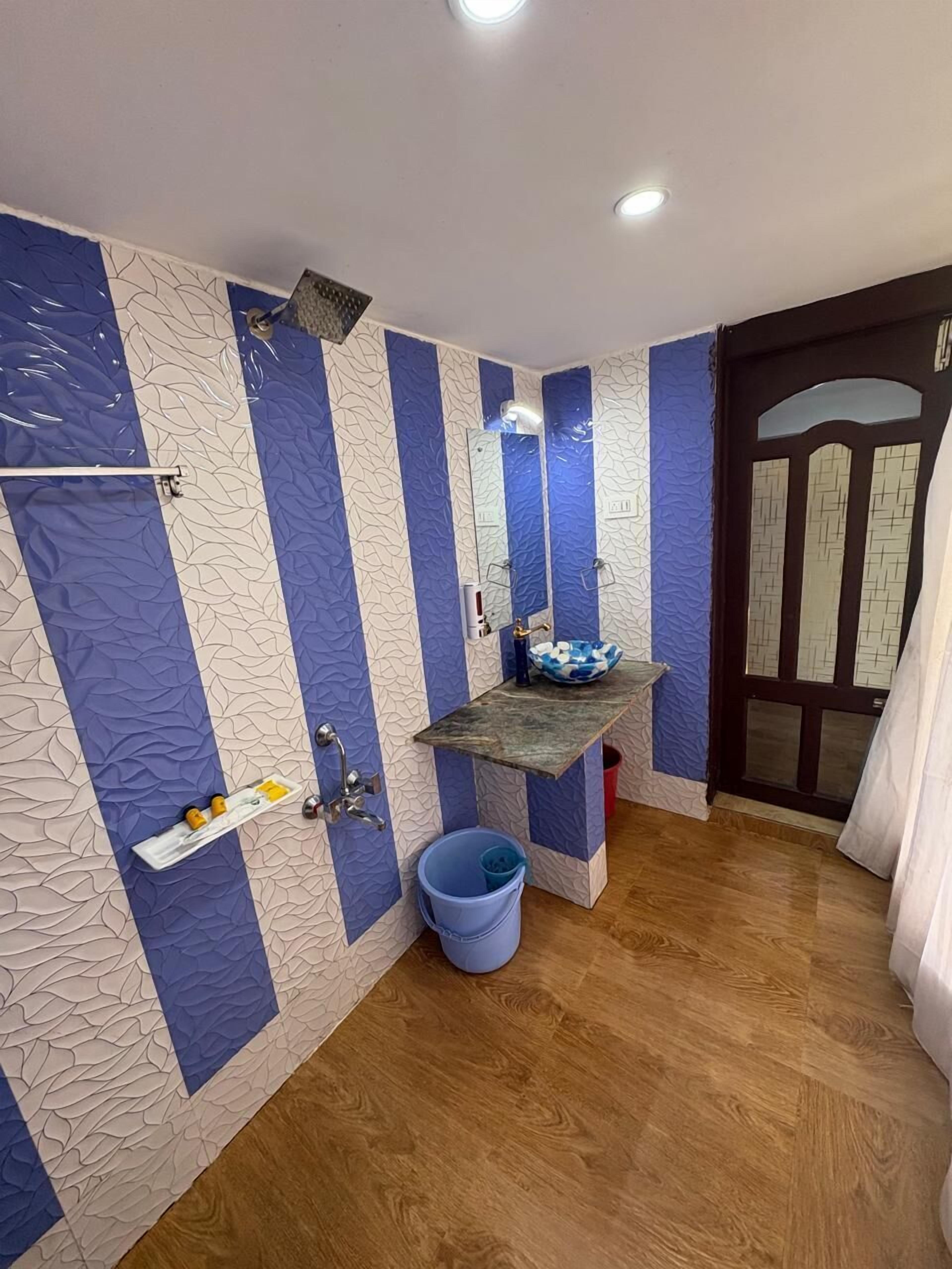 Um banheiro com parede azul e branca com textura, piso de madeira, pia com cuba azul, espelho e área de chuveiro.