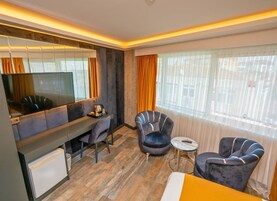 Quarto de hotel moderno com sofá, duas poltronas, uma mesa pequena, televisão e escrivaninha com cadeira.