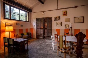 Um quarto com porta de madeira, uma mesa com cadeiras, um sofá e um abajur.
