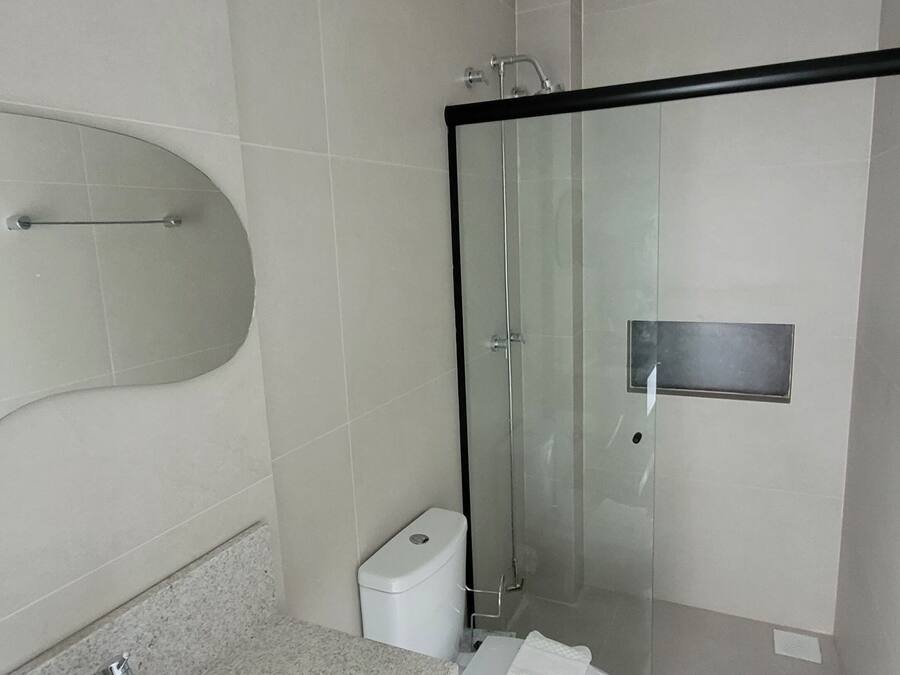Um banheiro moderno com box de vidro, vaso sanitário branco e bancada de granito com pia.