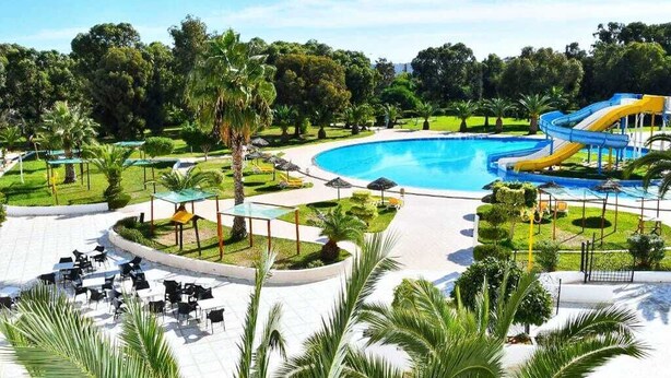 Piscina com toboágua, cercada por palmeiras e um espaço de lazer com cadeiras.