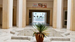 Um hall de entrada com piso de mármore, uma planta em vaso central, uma placa de spa e vista para a área do spa.
