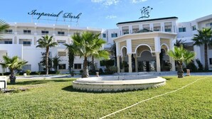 Um hotel com um pátio central, palmeiras e uma placa com a inscrição 'Imperial Park'.