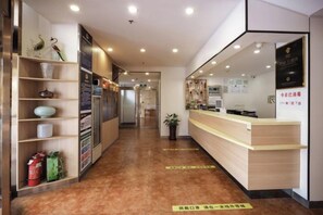 Uma área de recepção de hotel com balcão, bancada e um painel informativo fixado na parede.