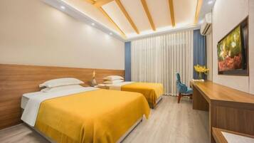 Quarto de hotel com duas camas, uma escrivaninha, uma cadeira e uma janela grande com persianas.