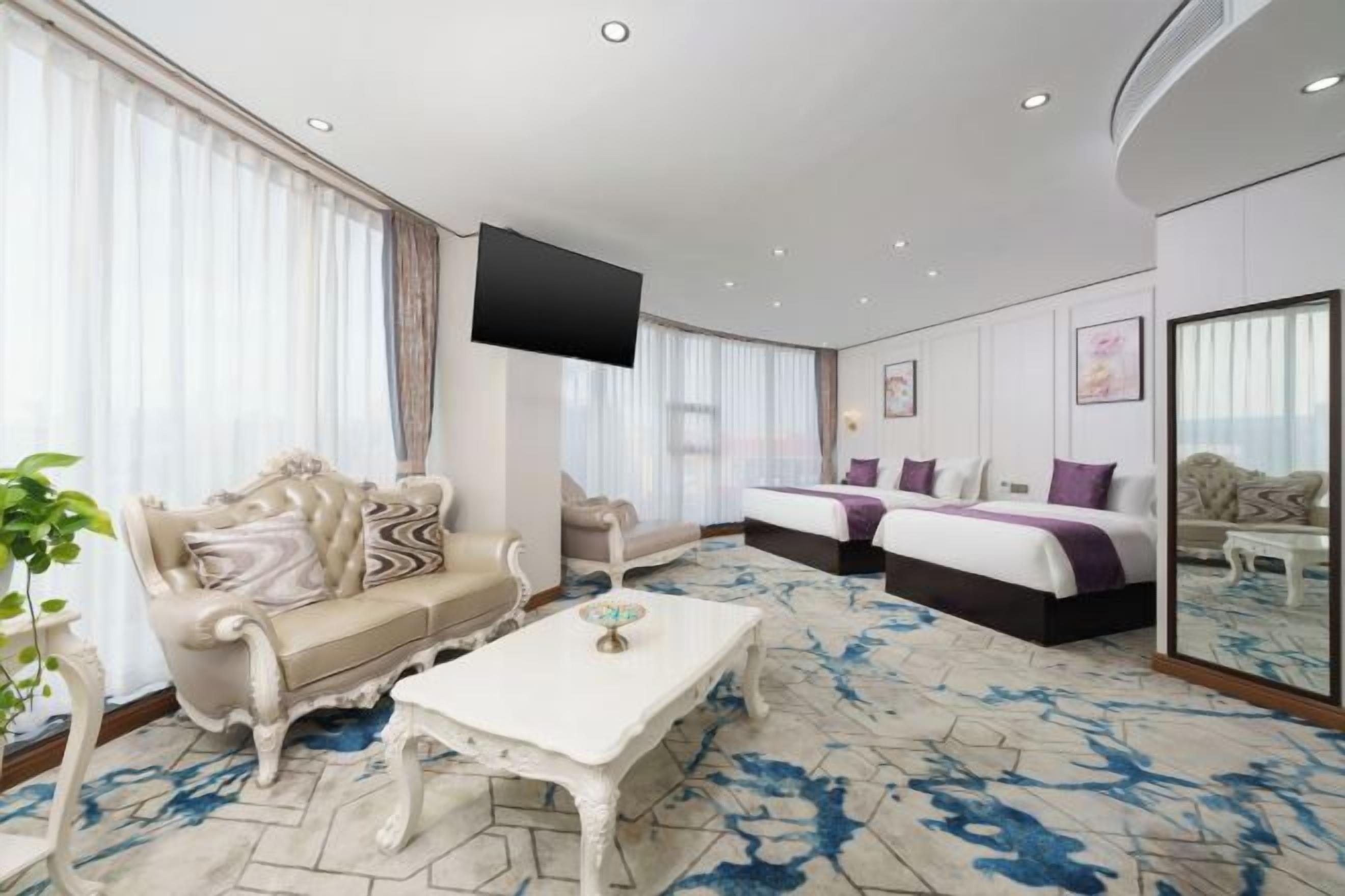 Quarto de hotel com sofá, cama, televisão e uma janela grande.