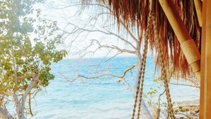 Um deck de madeira com hidromassagem e rede, com vista para uma praia.