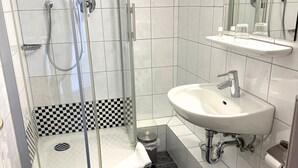 Um banheiro moderno com chuveiro em cabine de vidro, pia branca e painel de azulejos quadriculados.
