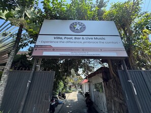 Placa anunciando Villa, Piscina, Bar e Música ao Vivo, com informações de contato e detalhes sobre a localização.