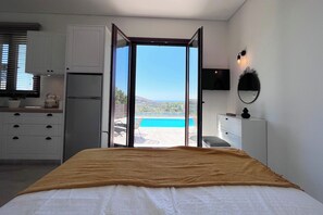Quarto com cama, vista para uma piscina e área de cozinha.