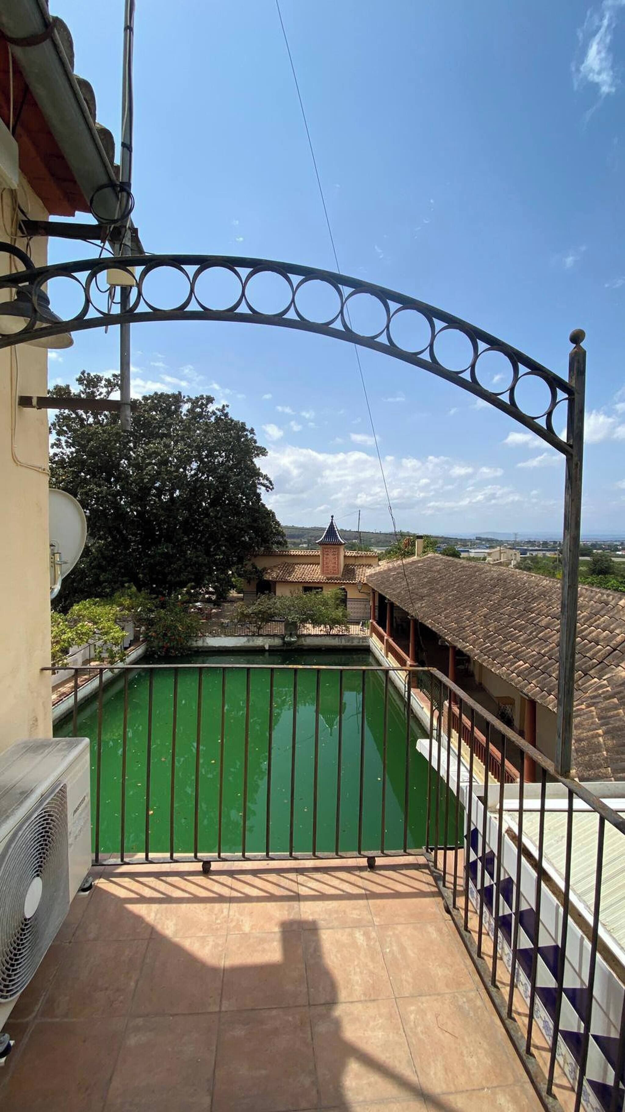 Uma varanda com vista para uma piscina verde, piso de azulejos e um portão de metal.