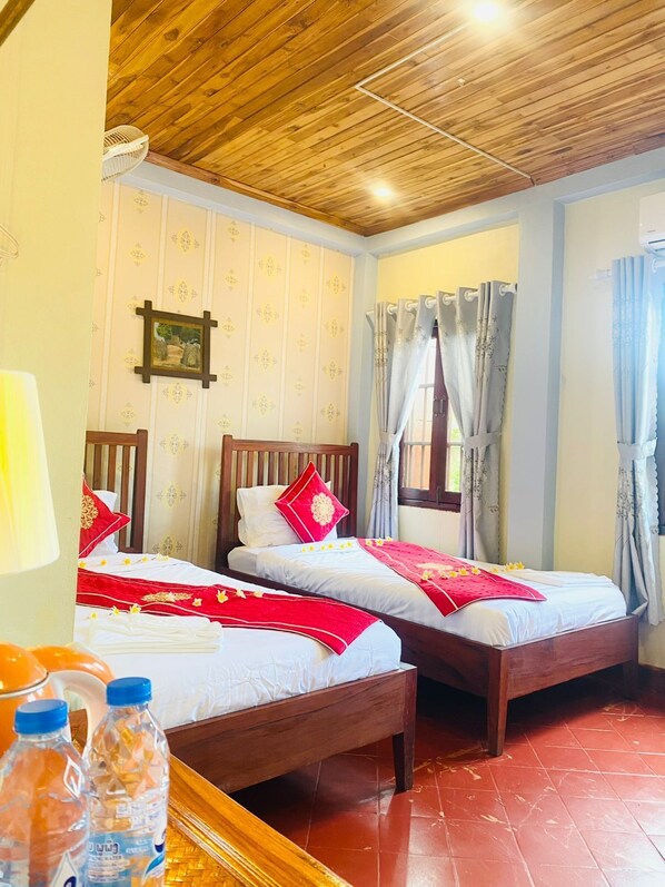 Quarto de hotel com duas camas de madeira, teto de madeira e janela com cortinas.