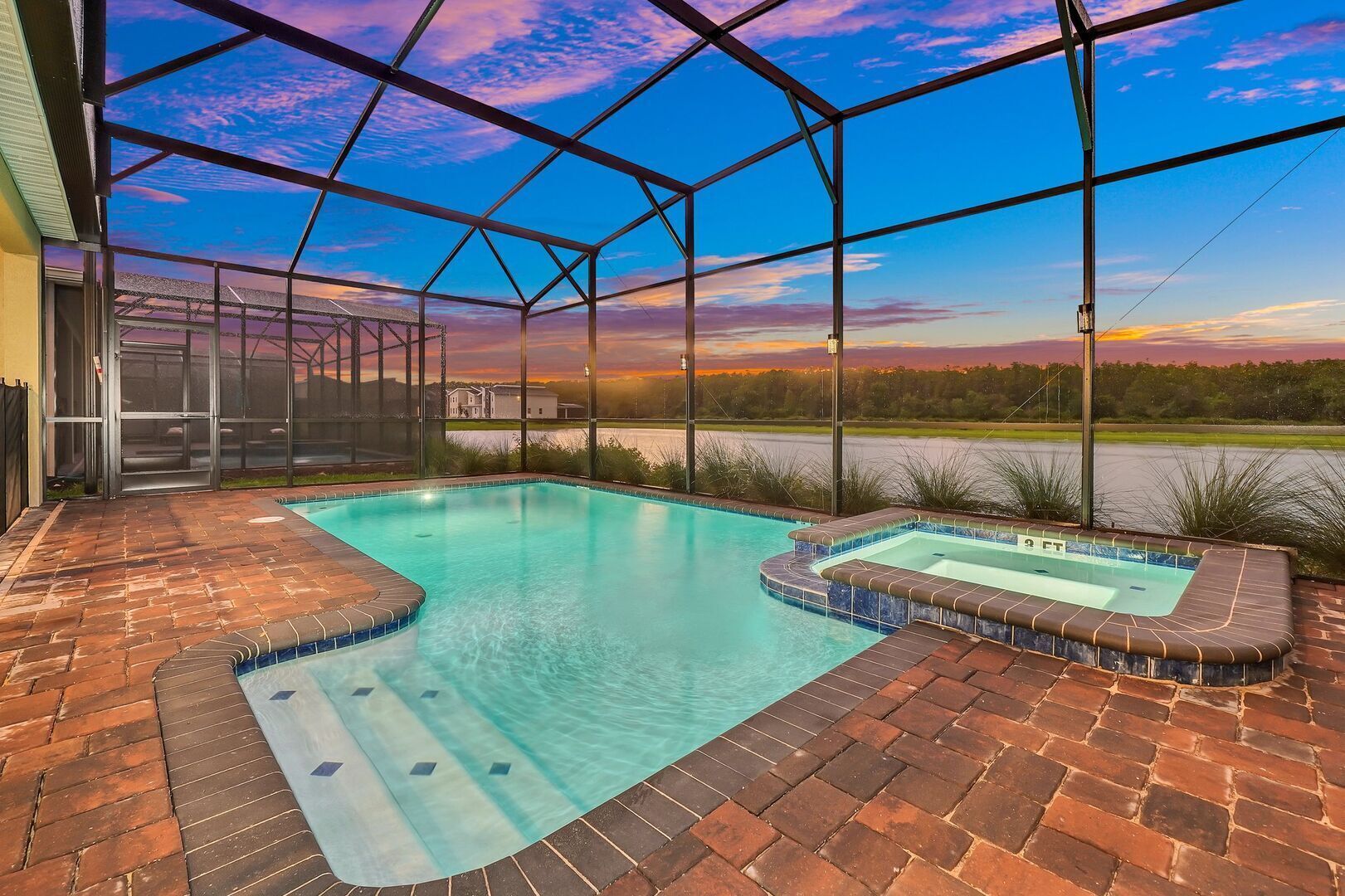 Piscina com hidromassagem, rodeada por um terraço coberto com vista para um lago e pôr do sol.